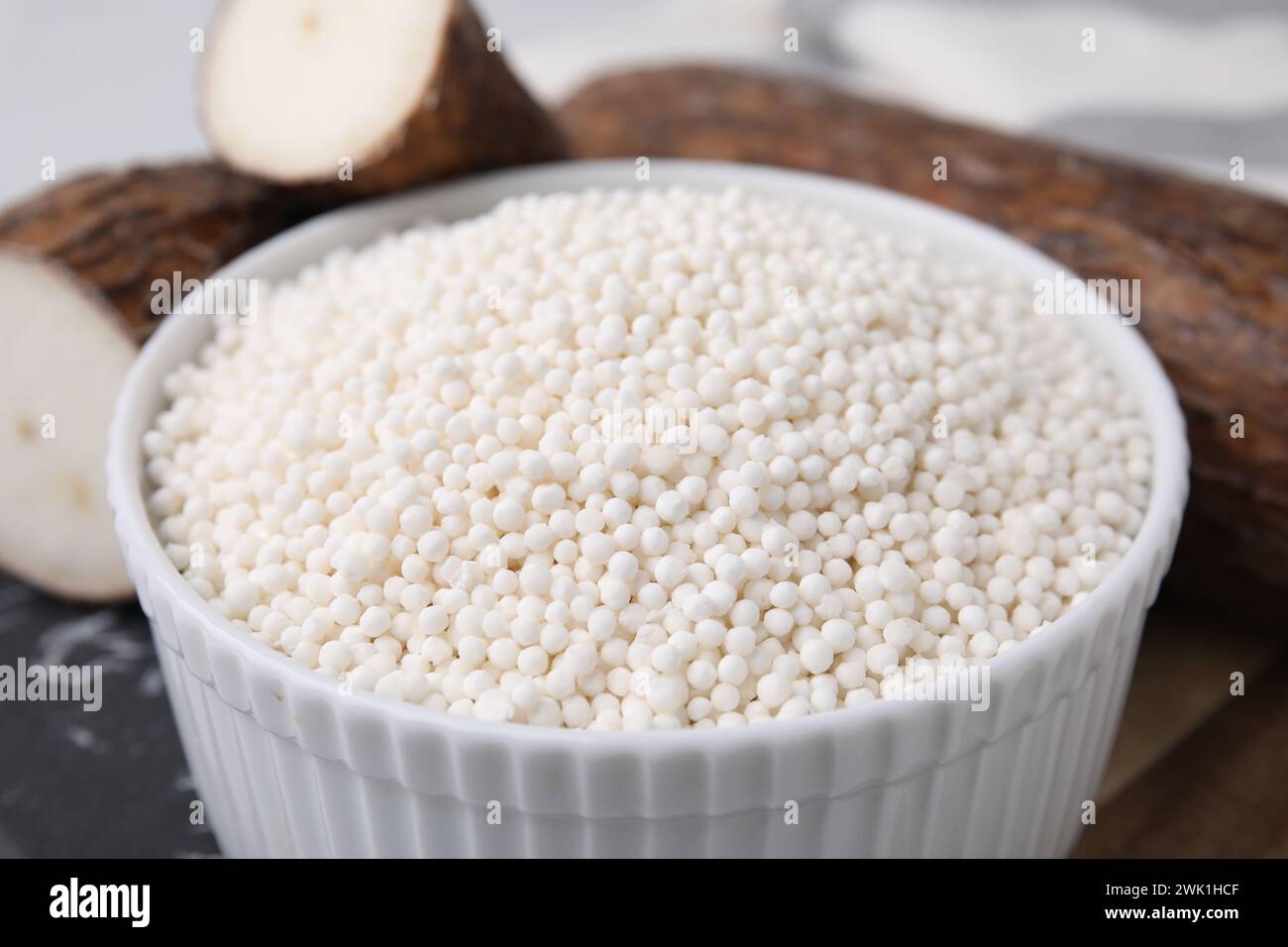 Tapioca pearls in bowl and cassava roots on table, closeup Stock Photo ...