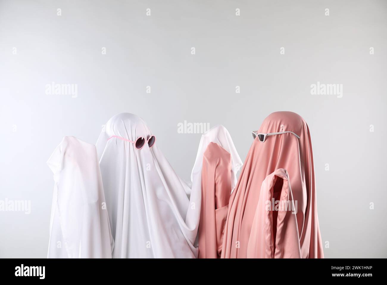 Glamorous ghosts. Women in color sheets with sunglasses on light grey ...