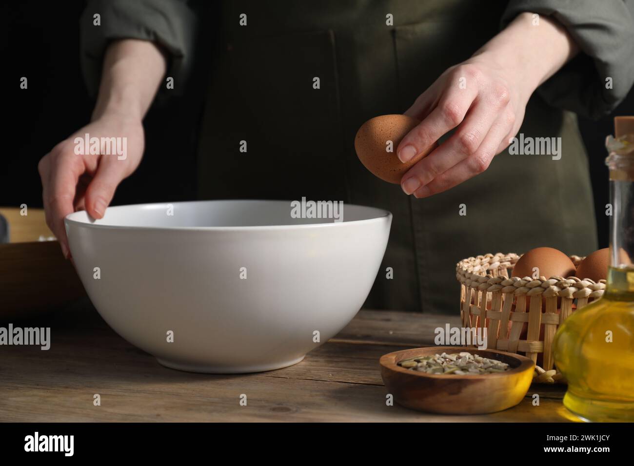 Making bread. Woman adding egg into dough at wooden table on dark background, closeup Stock ...