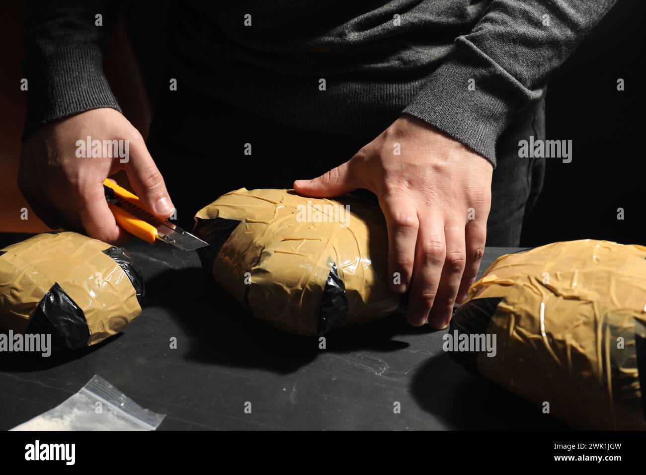 Smuggling and drug trafficking. Man opening package of narcotics with ...