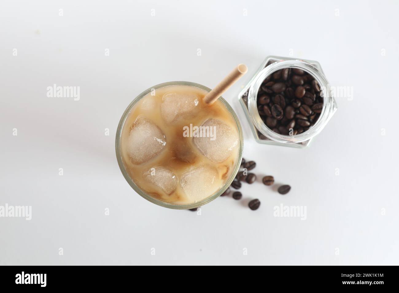 Iced coffee with milk in glass and jar of roasted beans on white ...