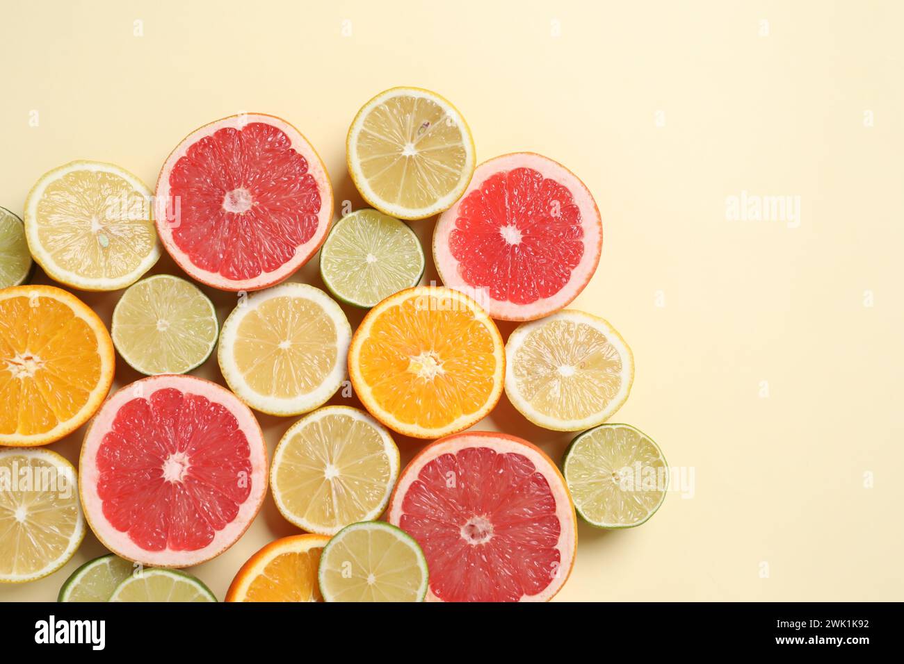 Different cut citrus fruits on beige table, flat lay. Space for text ...