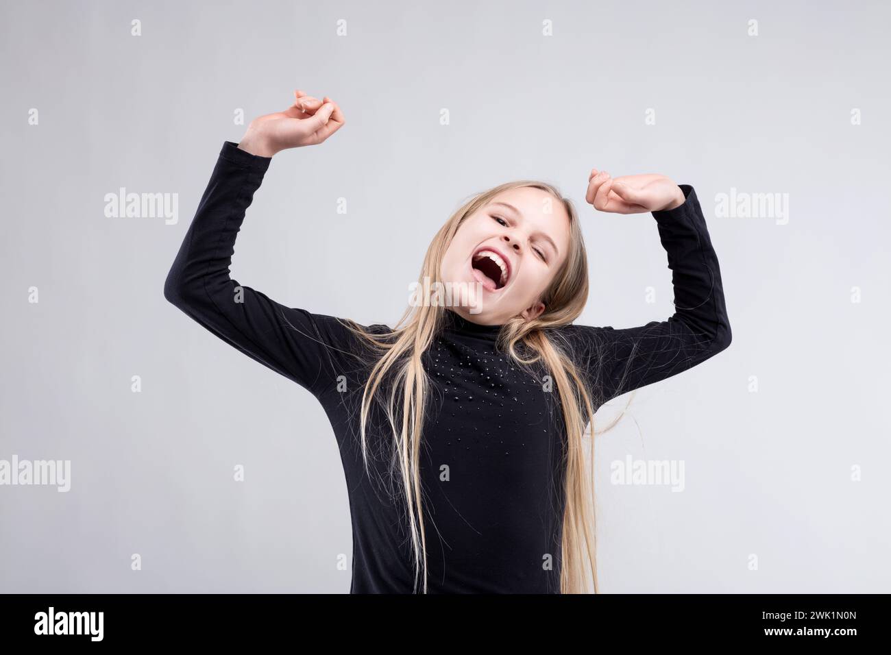 Exuberant young girl with arms raised celebrates joyfully, her laughter ...