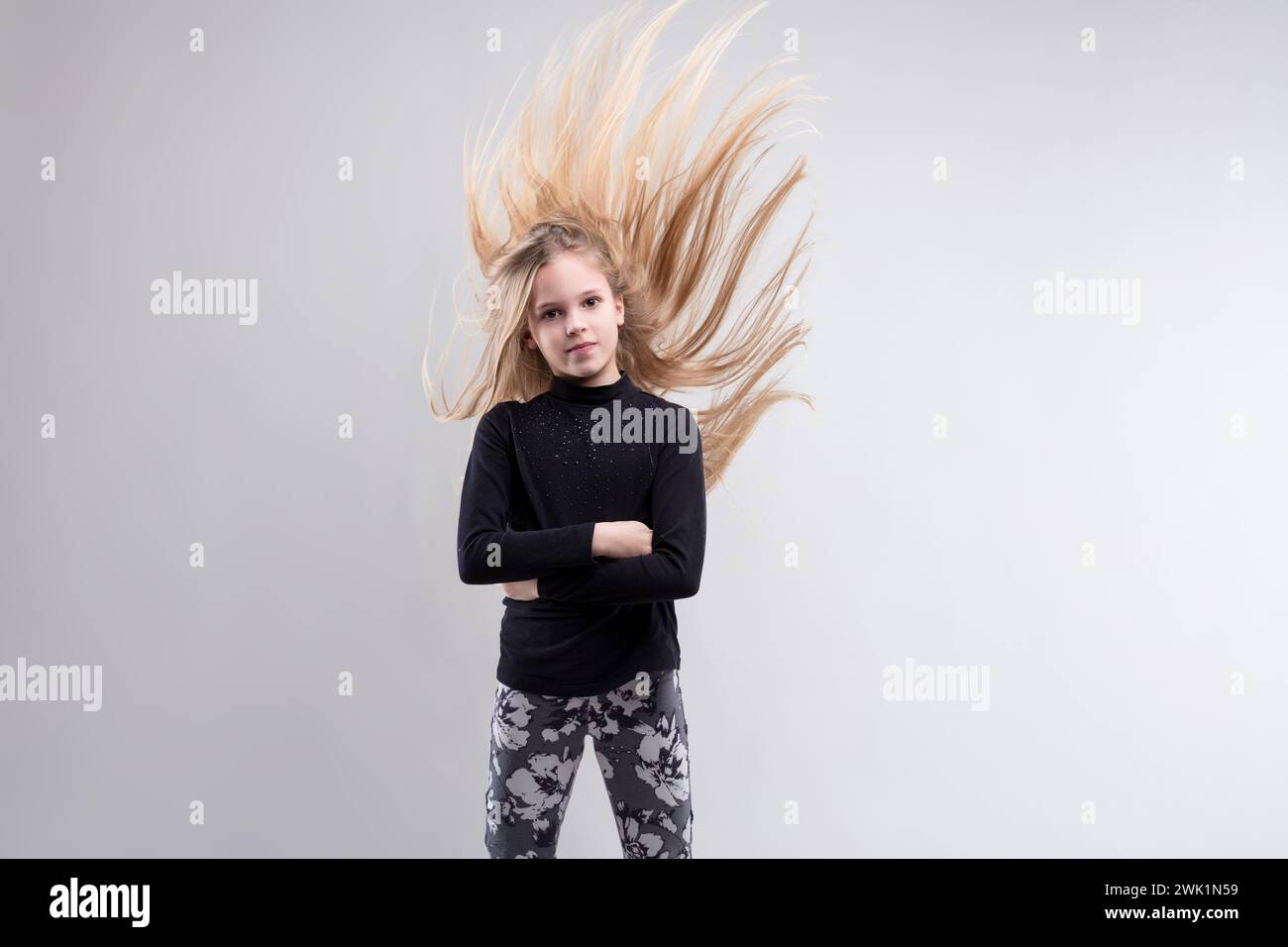 Young girl with dynamic hair motion, arms crossed, presents a mix of ...