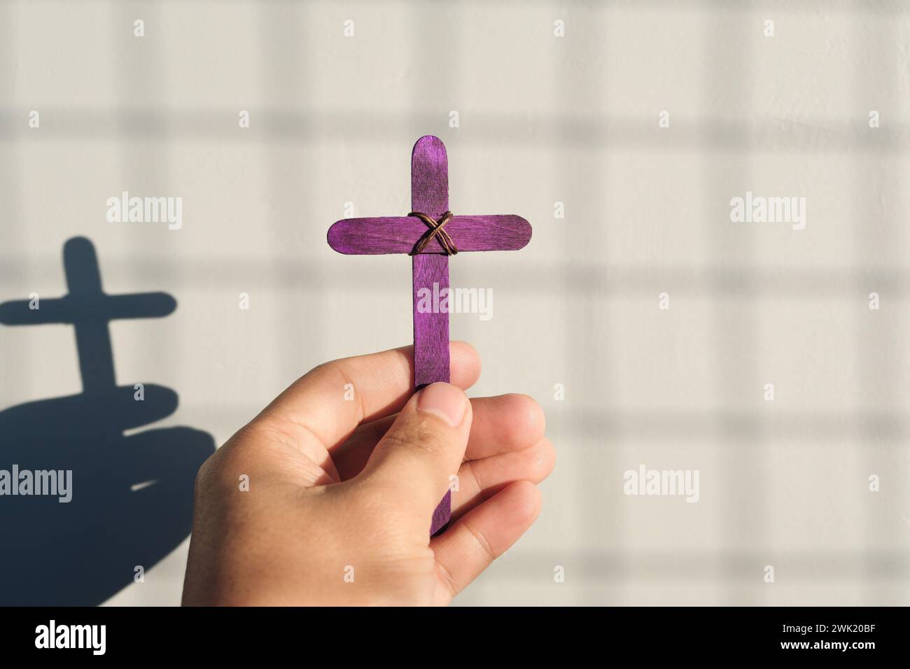 Male hand holding purple wooden cross with shadow. Christianity, faith ...
