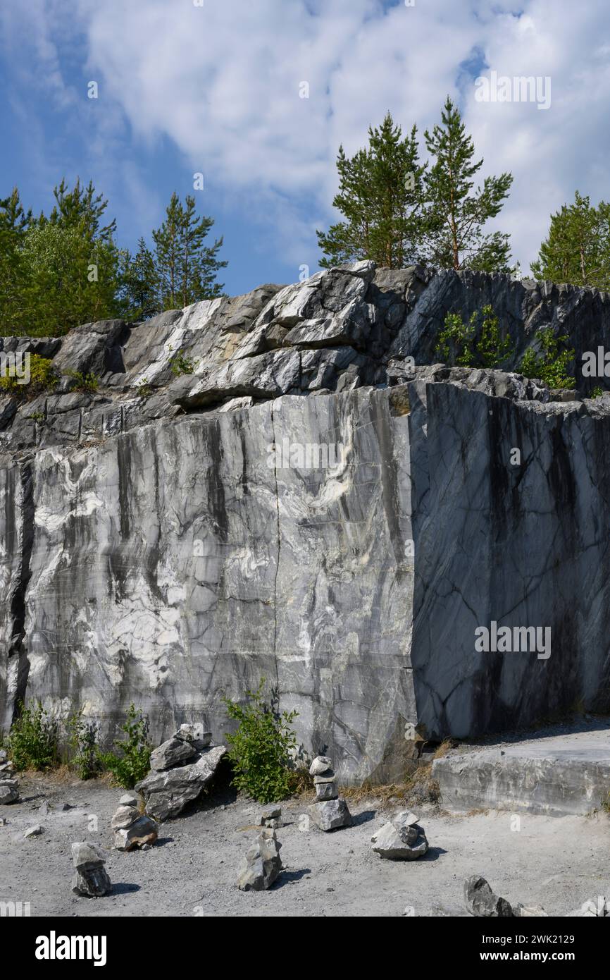Small pyramids of stones at the foot of a marble cliff with pine trees ...