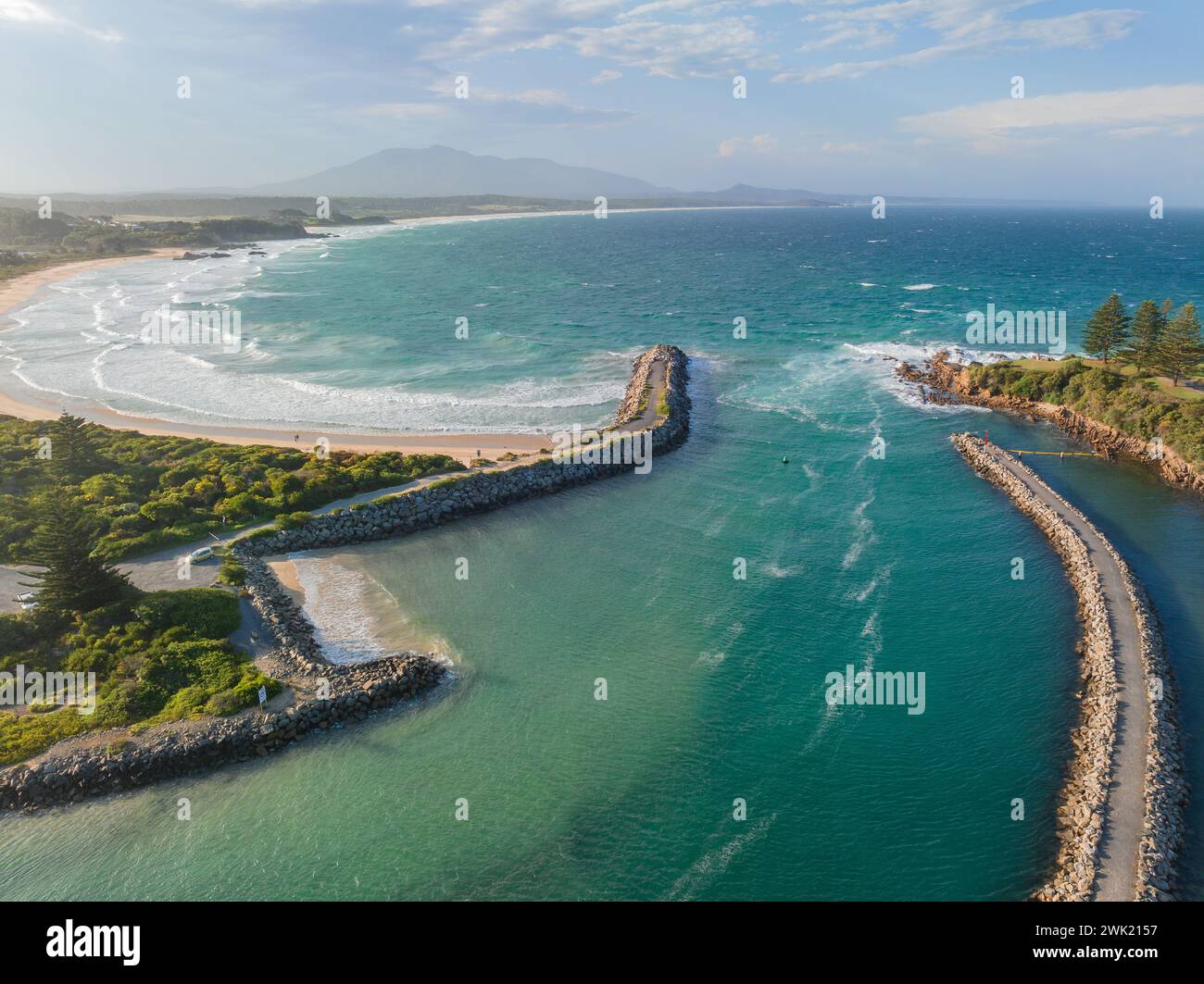 Aerial view of a river flowing out to sea between rocky breakwaters at ...
