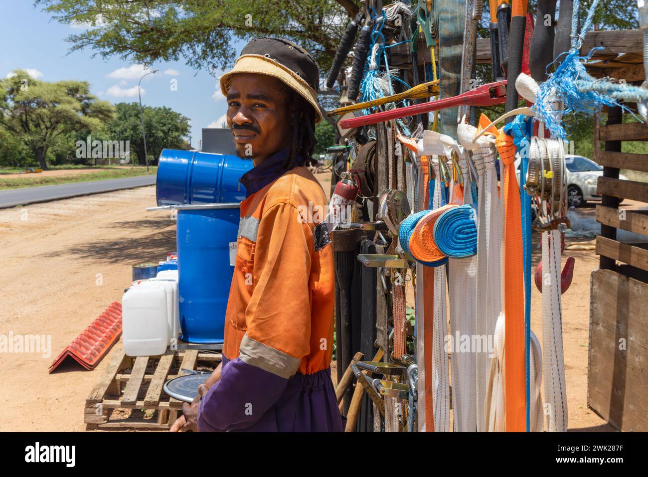 street vendor African man with braids selling hardware. belts and drums ...