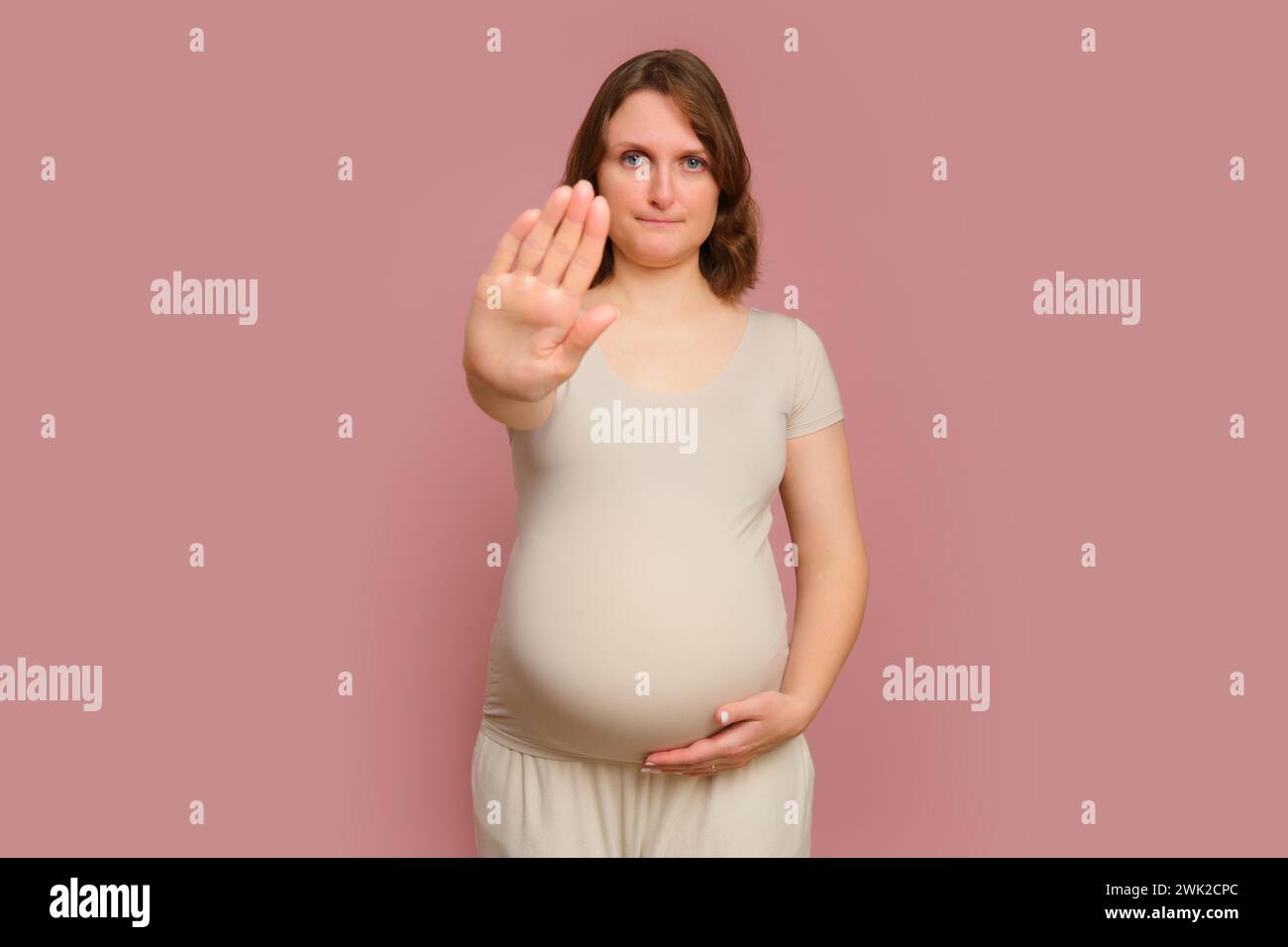 A pregnant woman shows a stop sign with her hand on a studio pink ...