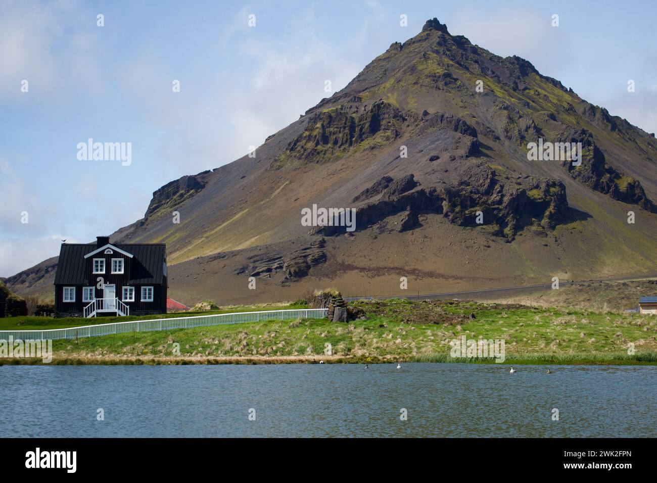 Remote black house on the lakeside at the foot of a mountain with green ...