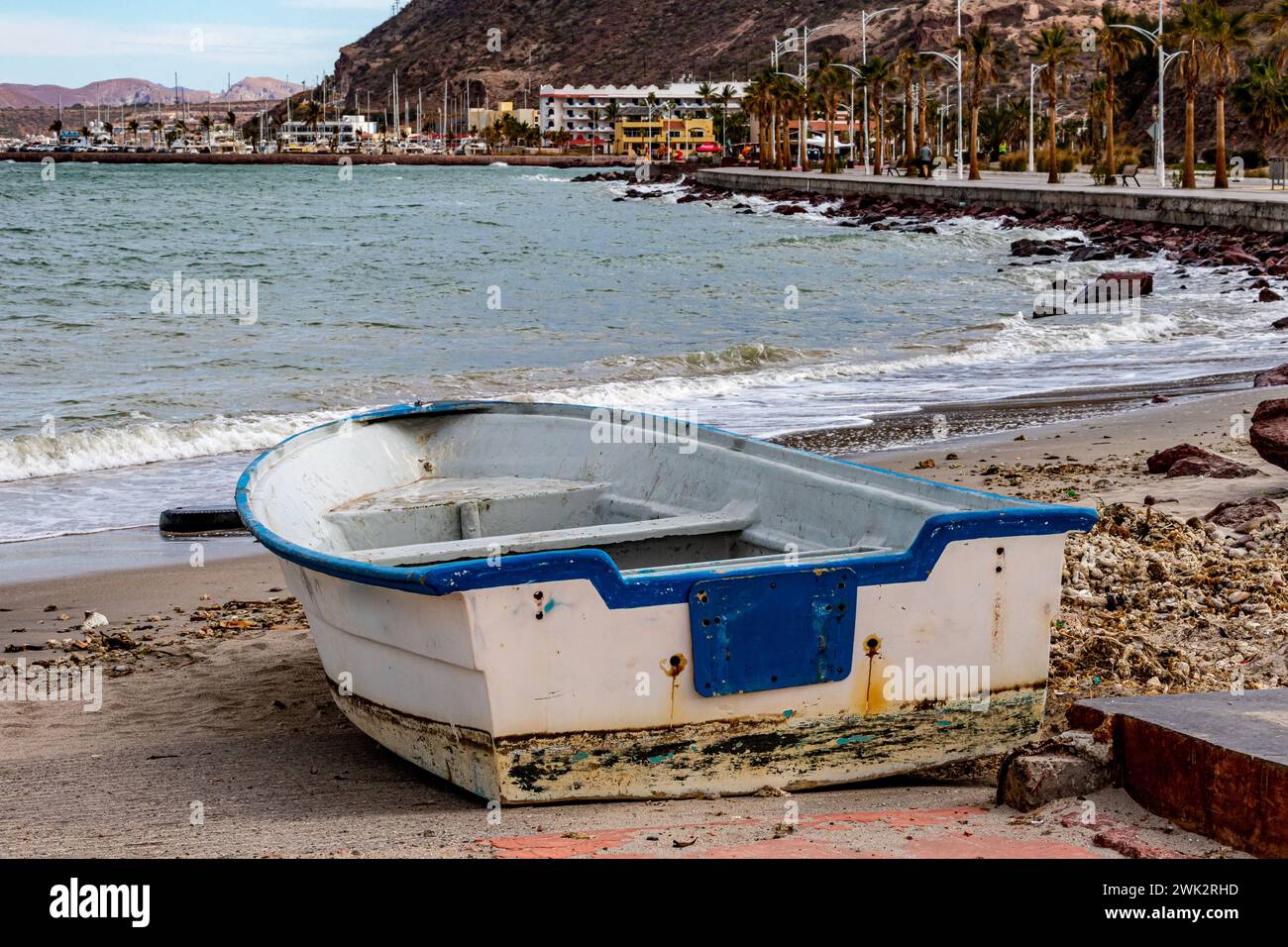 Old rowboat on sand on coastal beach with sea, boardwalk and marina in ...