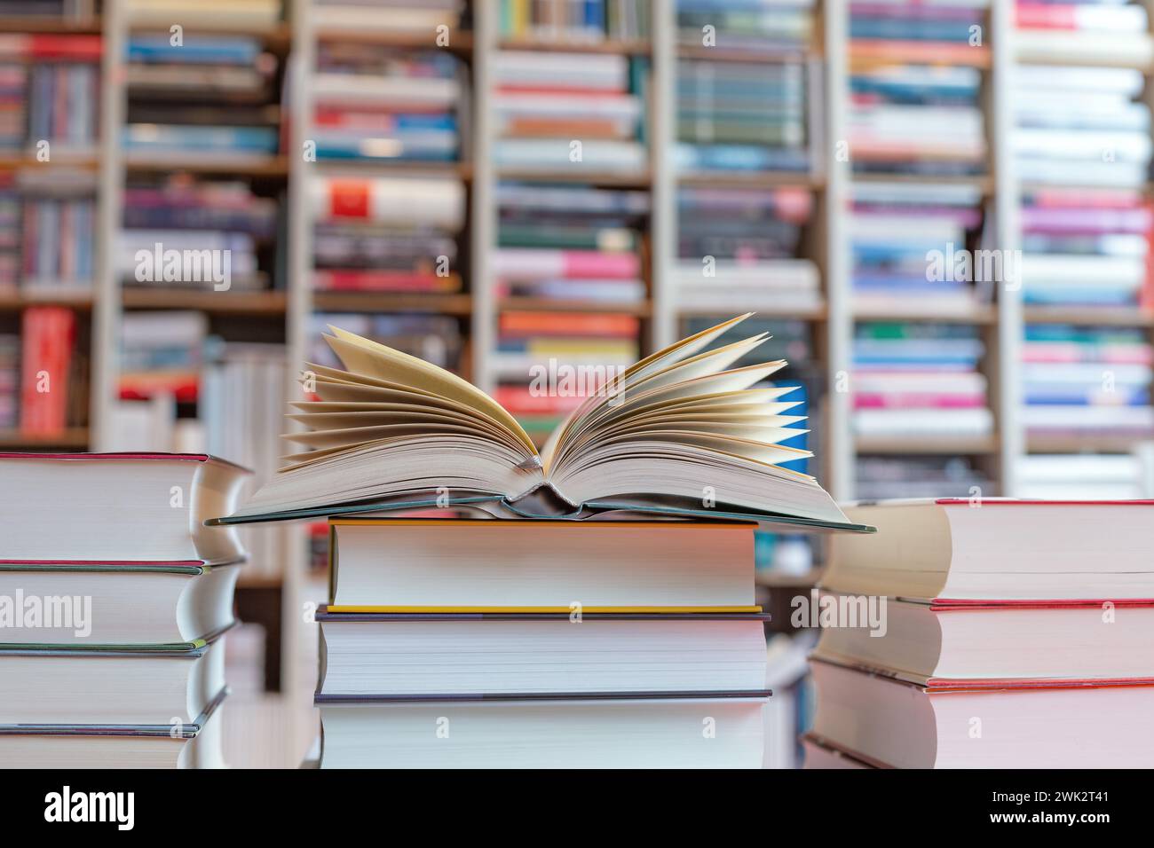 Open novel on stack of books in front of shelf Stock Photo - Alamy