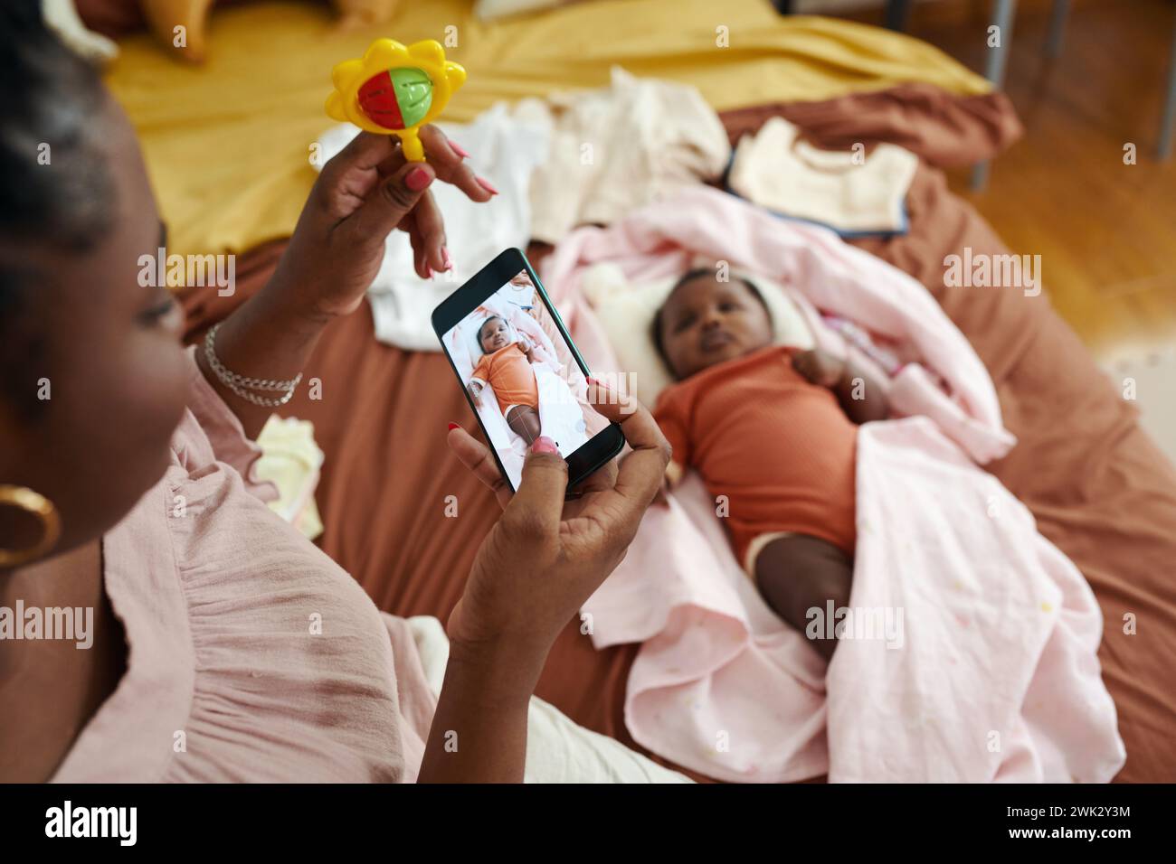 Mother shaking rattle to attract attention of baby and take photo for ...