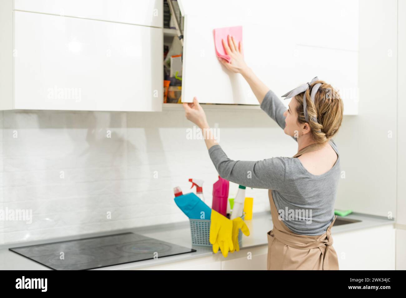 Woman cleaning and polishing the kitchen worktop with a spray detergent ...