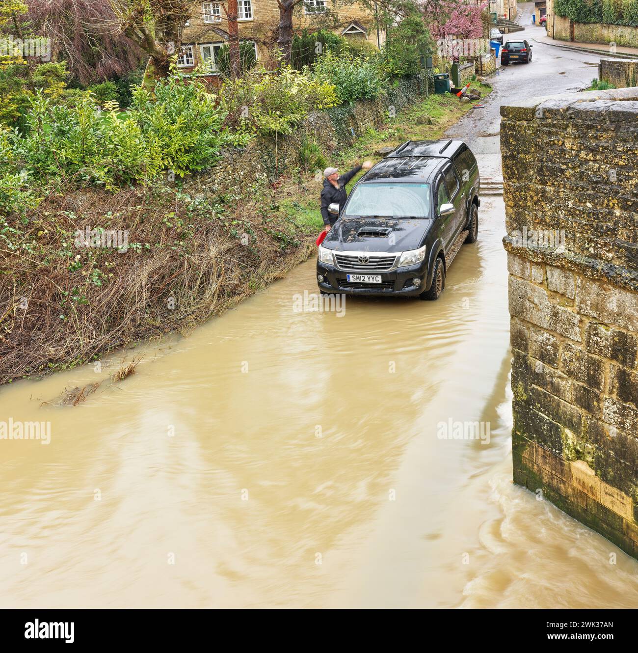 A man washes his dirty car with the muddy flood water of the river Ise ...