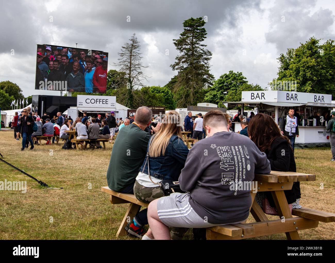 People sat around benches with catering vans serving food drink and ...