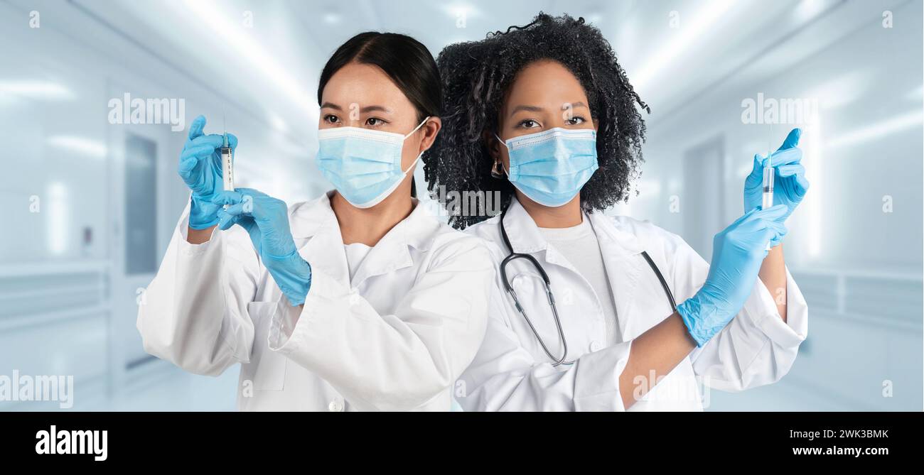 Two diverse female healthcare workers in white coats and blue gloves ...
