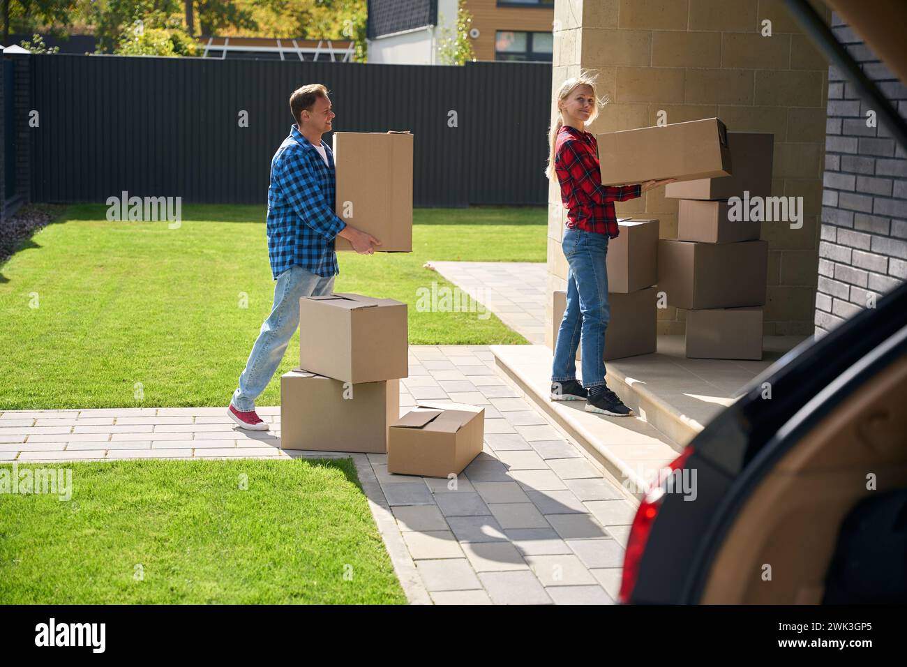 Cheerful couple carrying and arranging boxes on house doorstep Stock ...