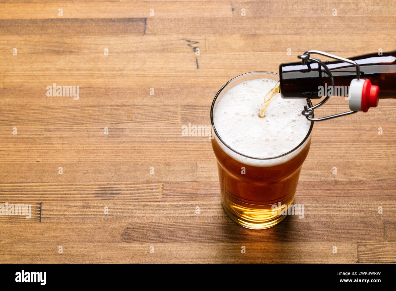Craft beer is pouring from swing top bottle into nonic pint glass ...