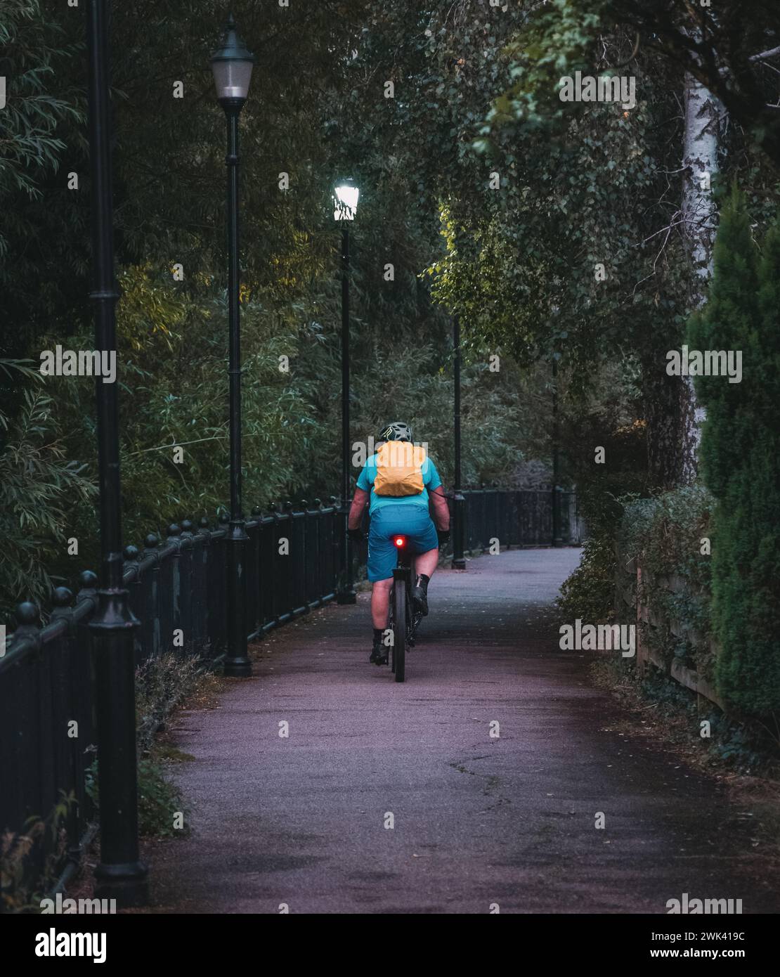 Cyclist riding bike on sidewalk between two lamp posts Stock Photo - Alamy
