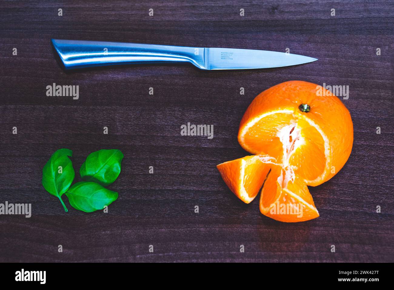 Sliced fresh mandarin, basil leaves and silver kitchen knife arranged ...
