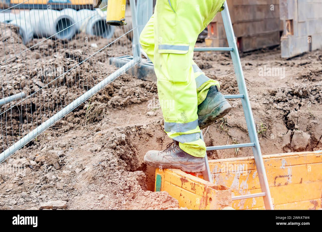 Groundworker builder using steps ladder to get out of the deep drainage ...
