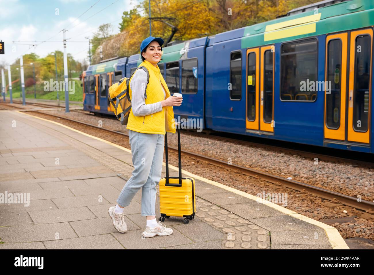 Happy young tourist woman with small yellow luggage at the train ...