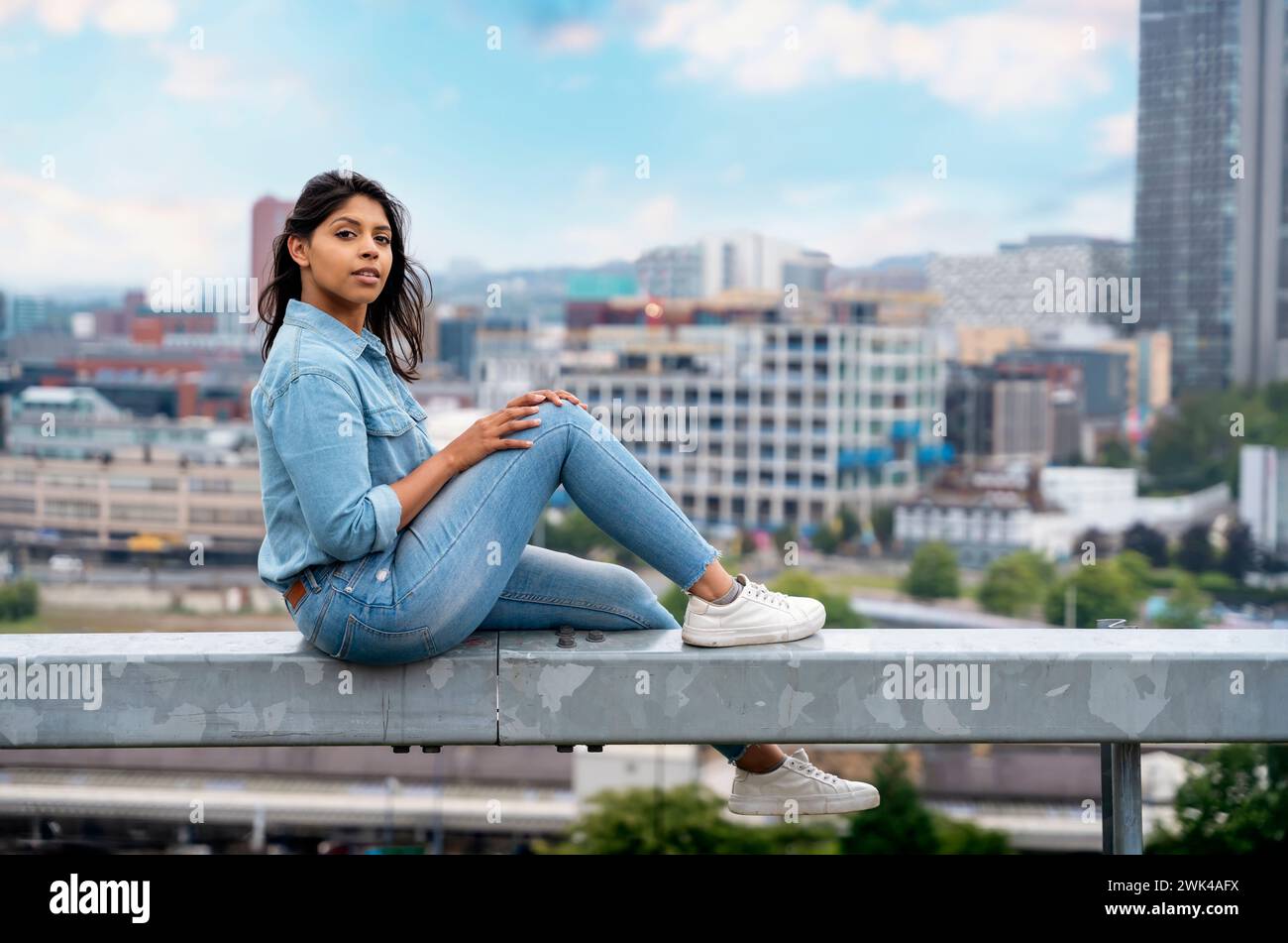 Portrait of a beautiful Indian woman sitting on the barrier in front of ...