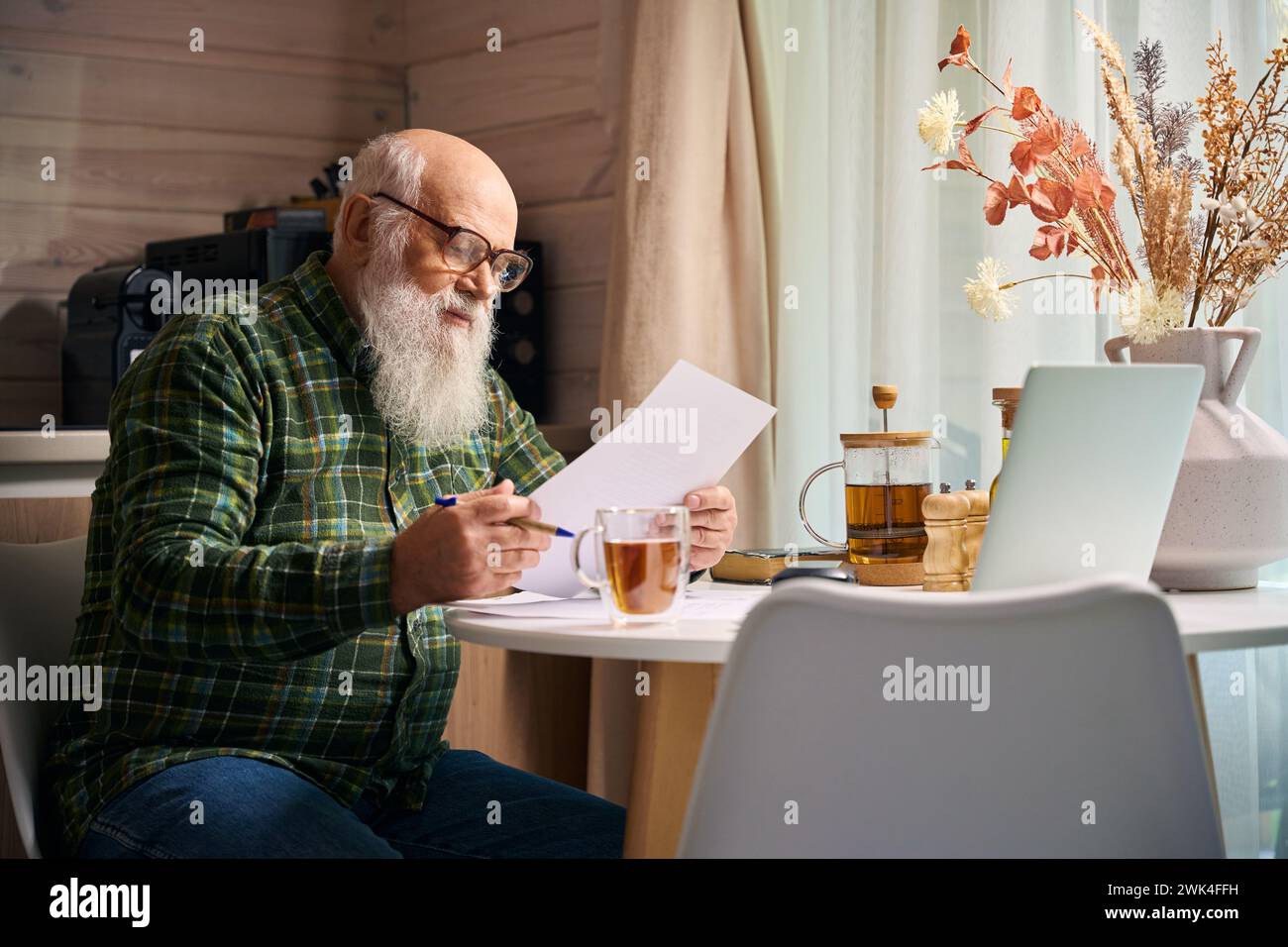 Grandfather sitting down at kitchen table with laptop and documents ...