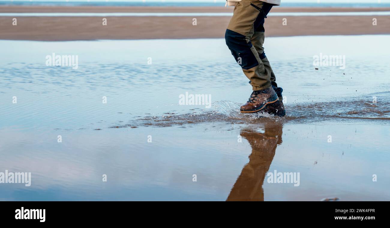 An energetic man in waterproof hiking boots walking along sea shore ...