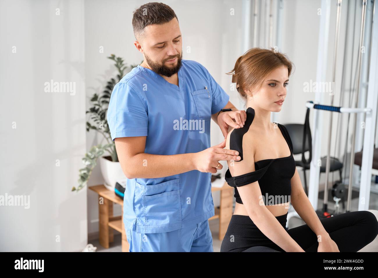 Doctor at a kinesiotherapy clinic applies tape to patients shoulder ...