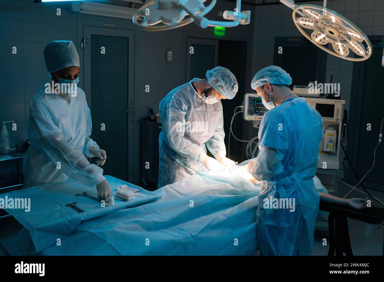 Skilled cooperating team of doctors and surgeons processing surgical operation in dark operating ...