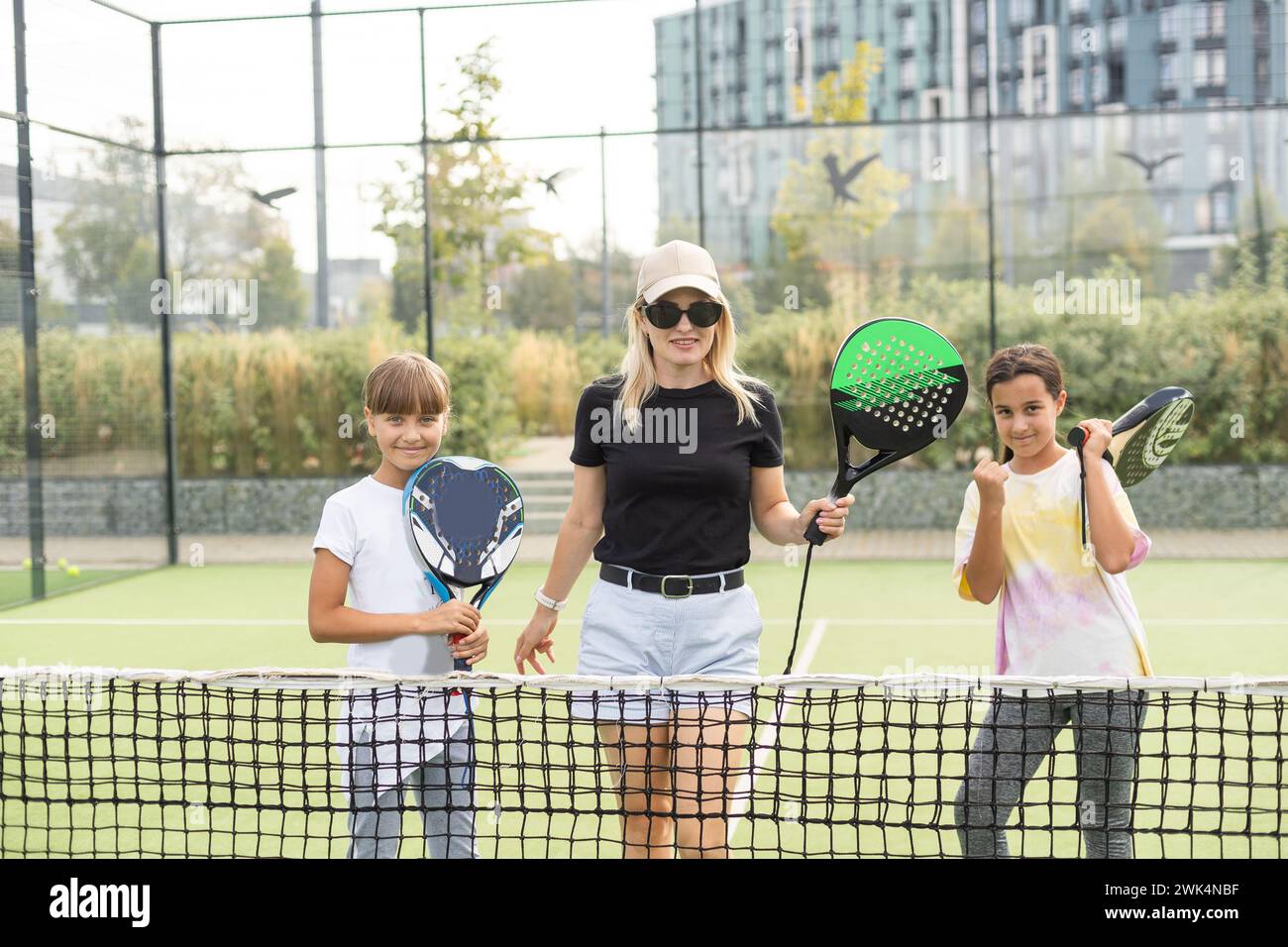Young sporty woman with children playing padel game in court on sunny ...