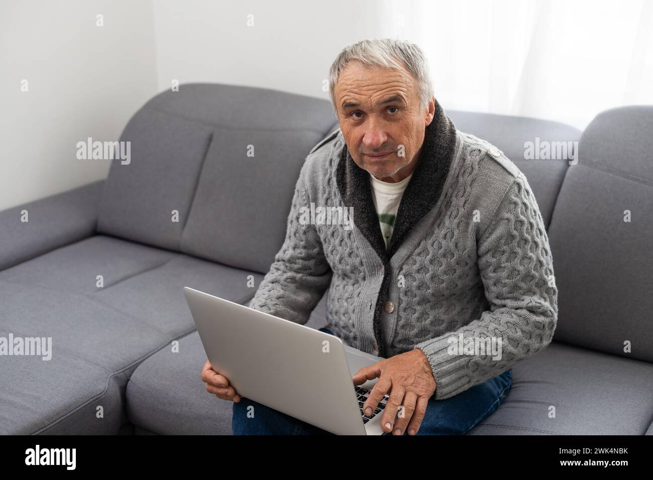 Older man sitting on sofa, smiling at computer screen at home Stock ...