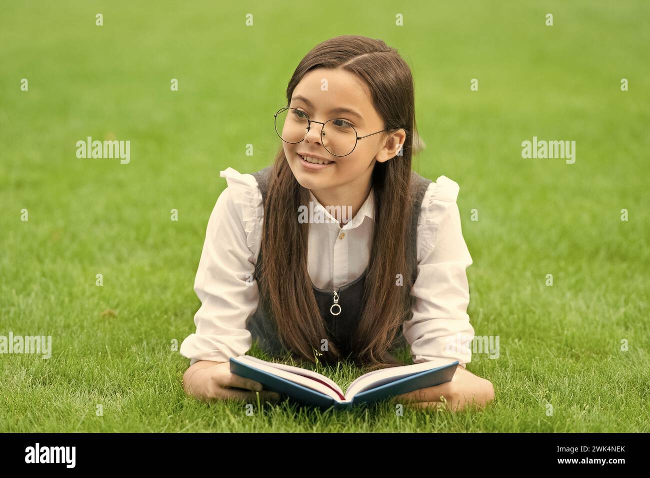 Portrait of happy teen girl reading school book lying on grass ...
