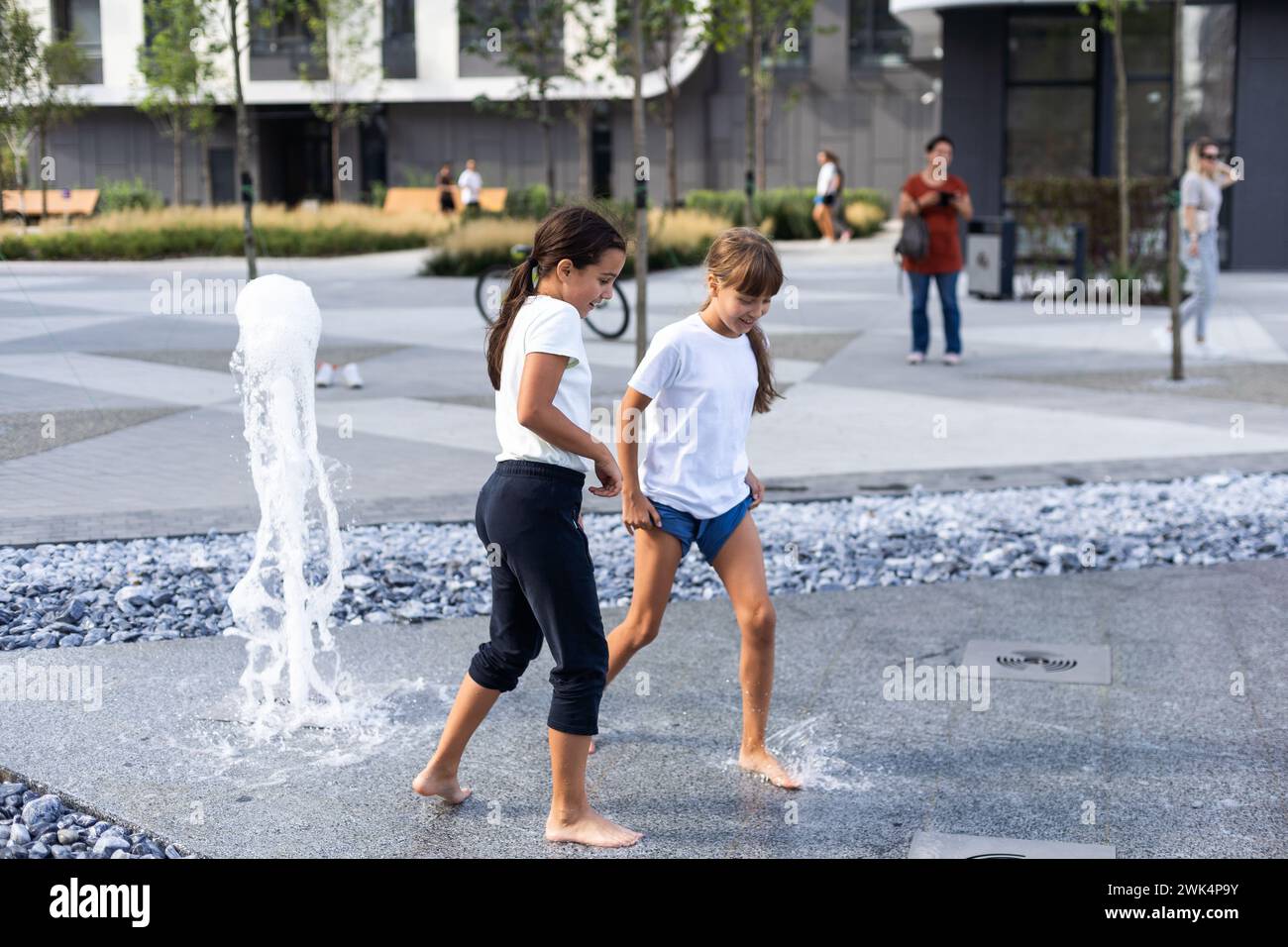 Cheerful young teen girl in city fountain, girl in wet clothes is ...