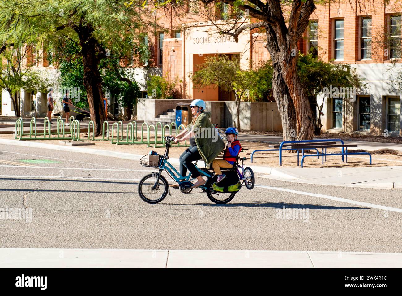 Woman riding a bicycle with her child in a child seat behind her and a ...