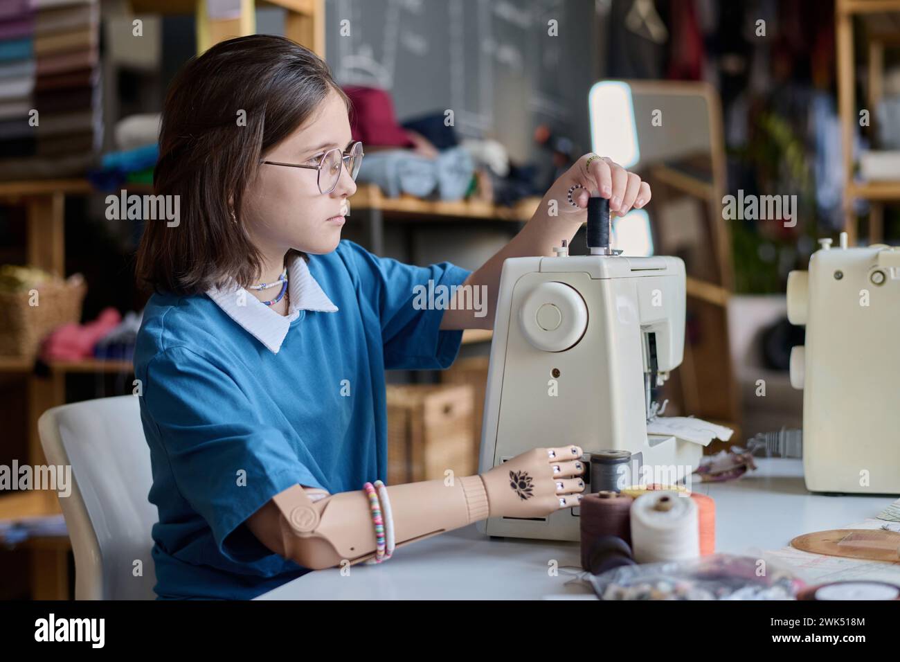 Side view portrait of teenage girl with prosthetic hand using sewing ...