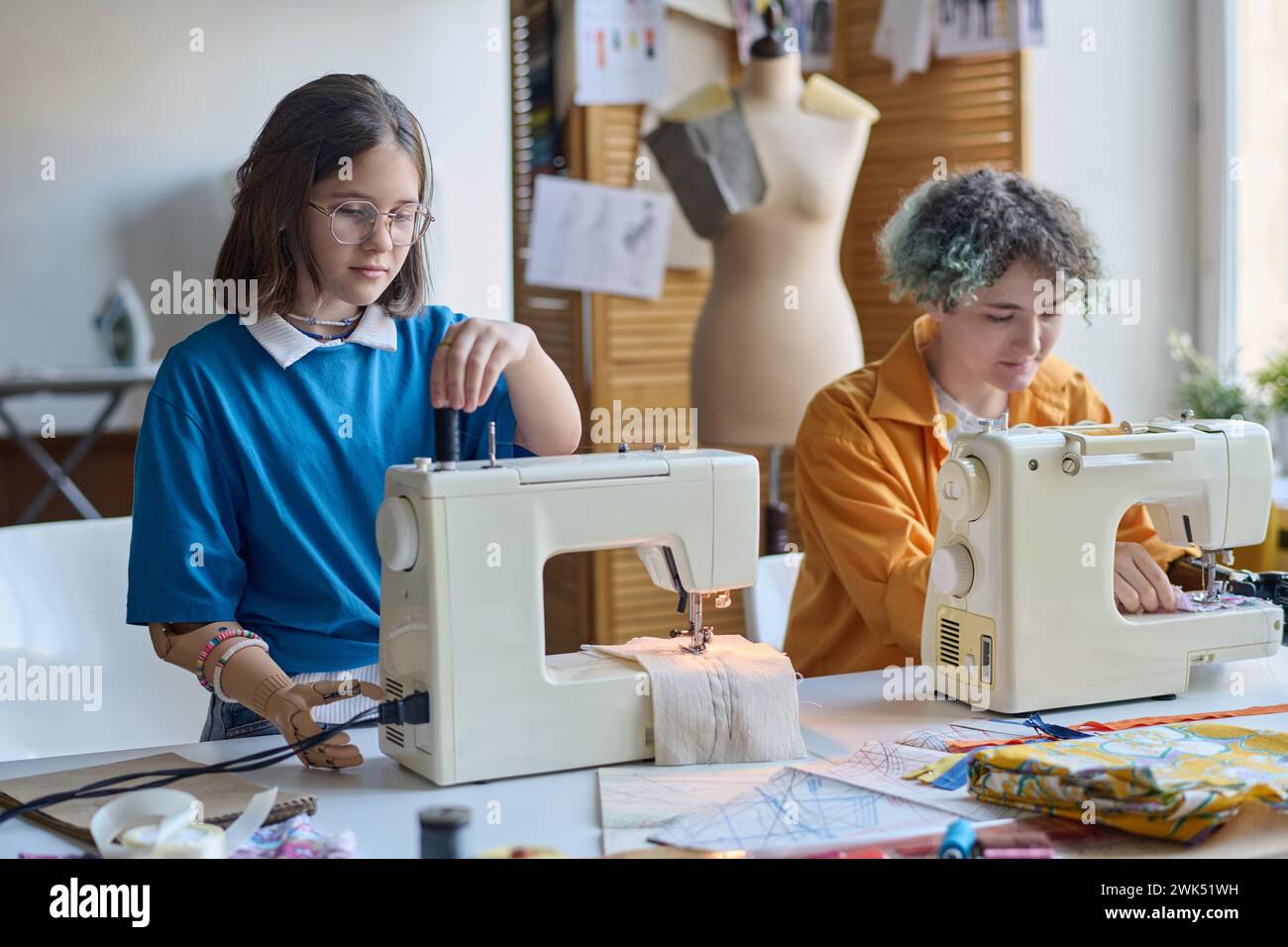 Portrait of two young girls with disability using sewing machines in ...