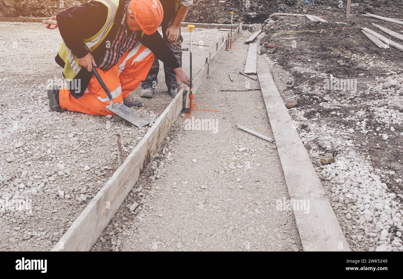 Groundworker in orange safety hi-vis trousers fixing a timber along ...