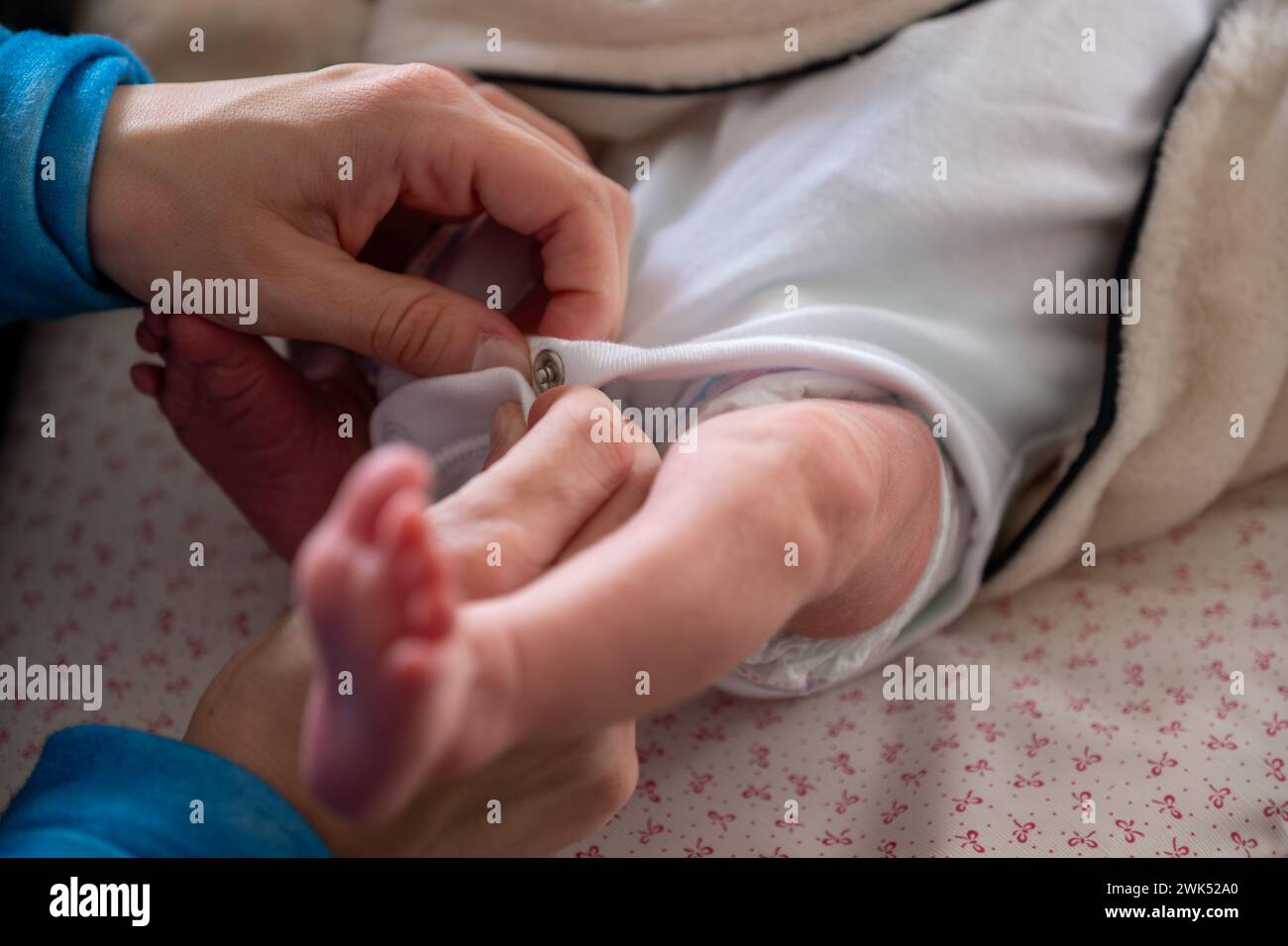 mother changing pampers for her baby , holding his tiny leg while ...