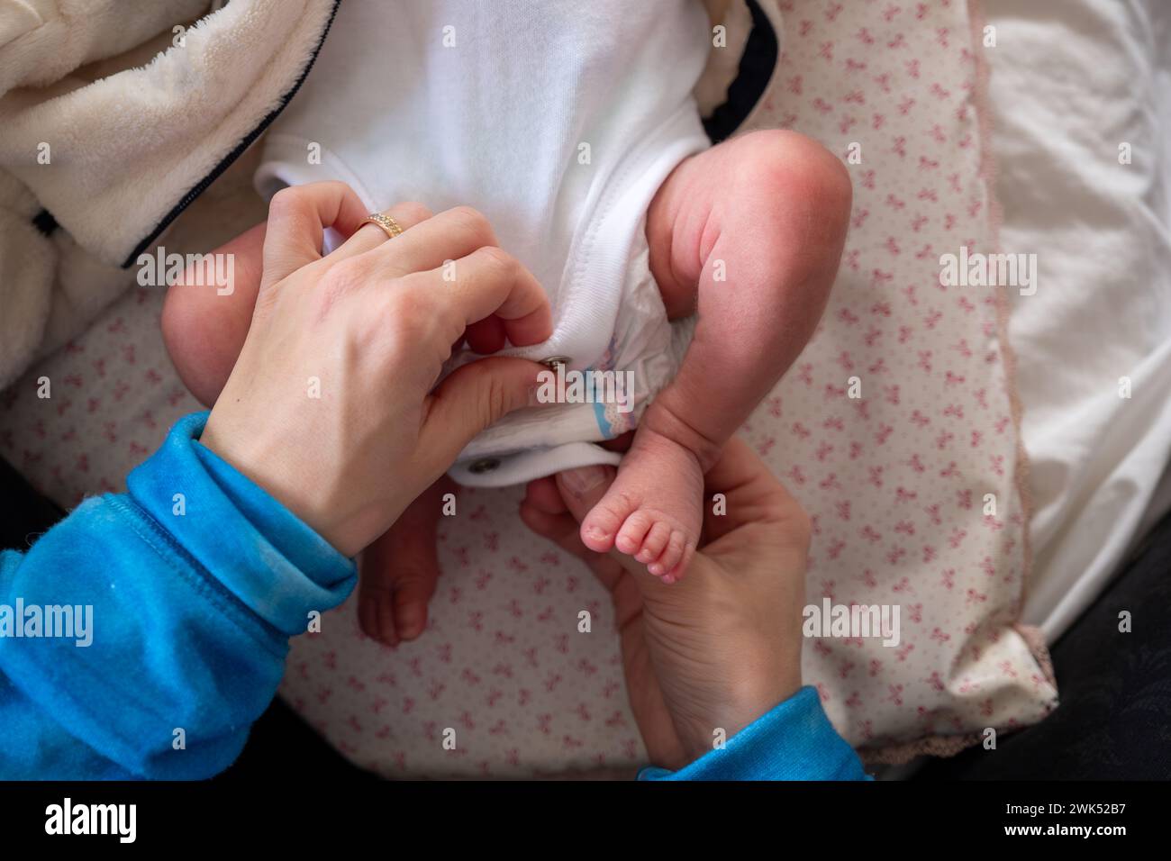 mother changing pampers for her baby , holding his tiny leg while ...