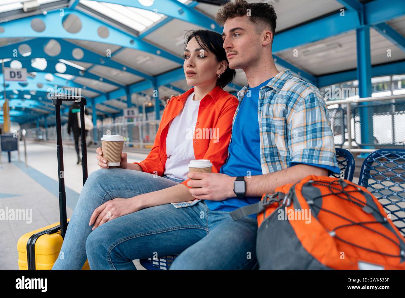 a young unhappy couple traveling together, waiting for a bus with ...