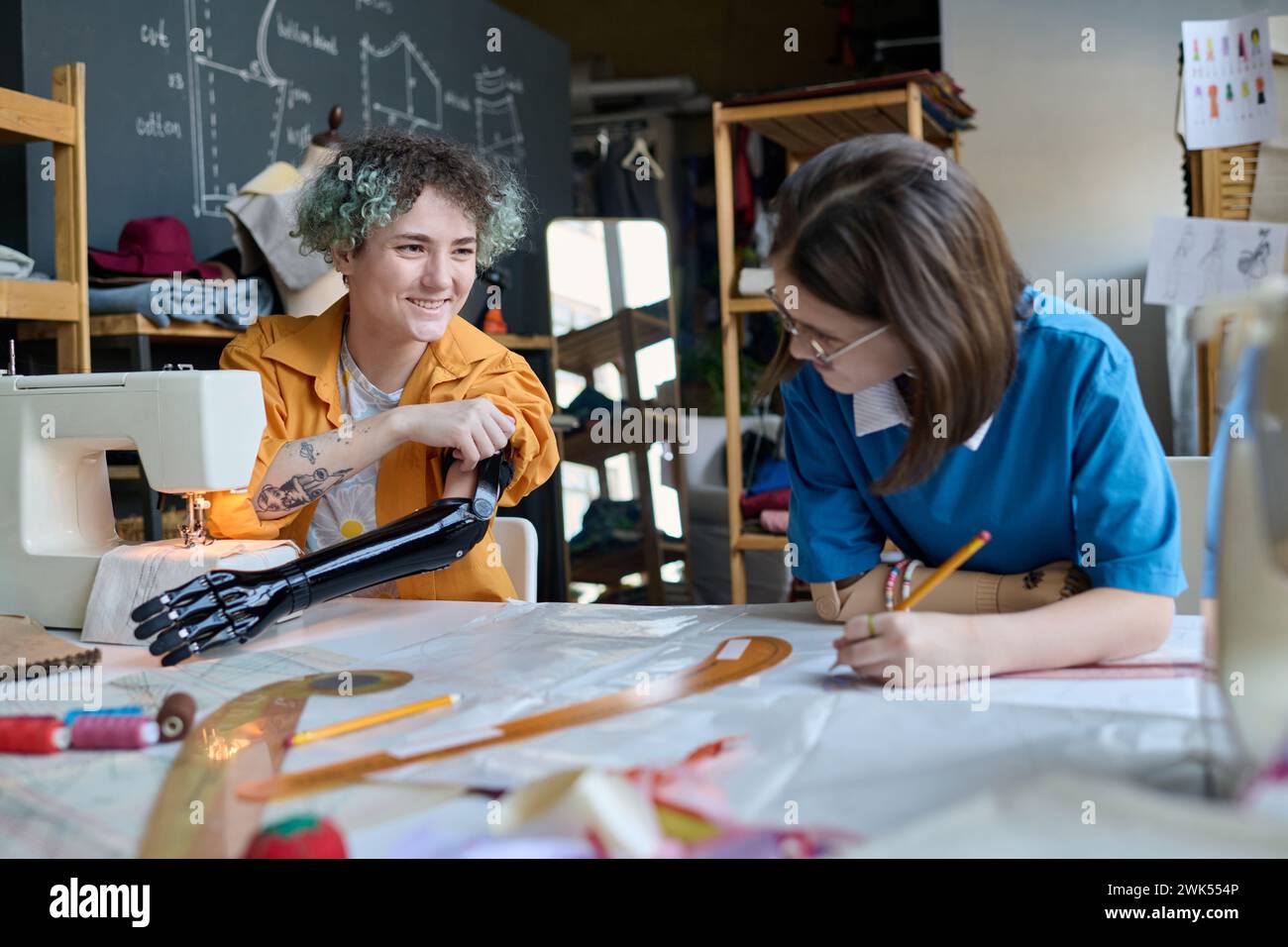 Portrait of two smiling teenage girls with prosthetics sewing clothing ...