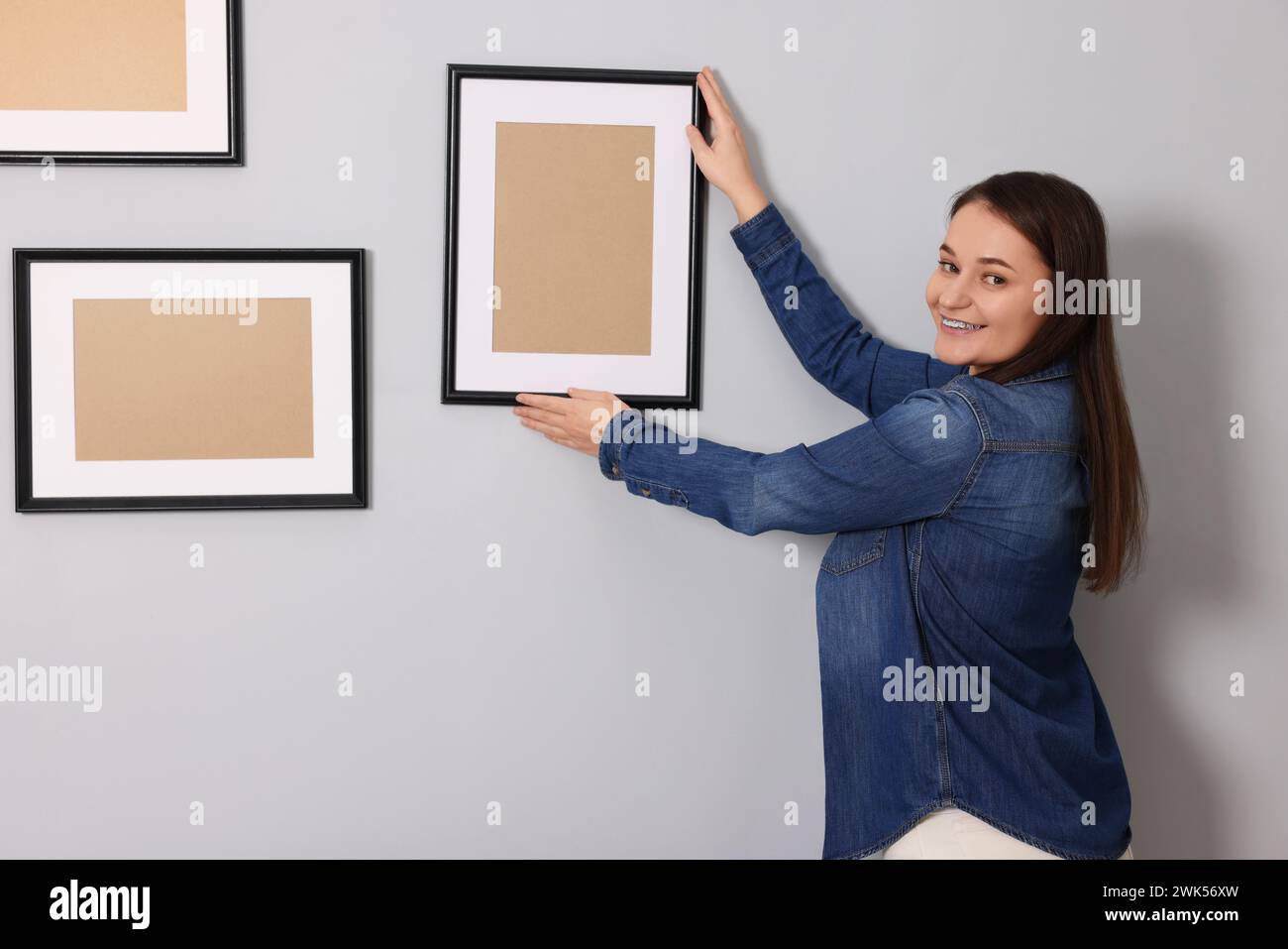 Woman hanging picture frame on gray wall Stock Photo - Alamy