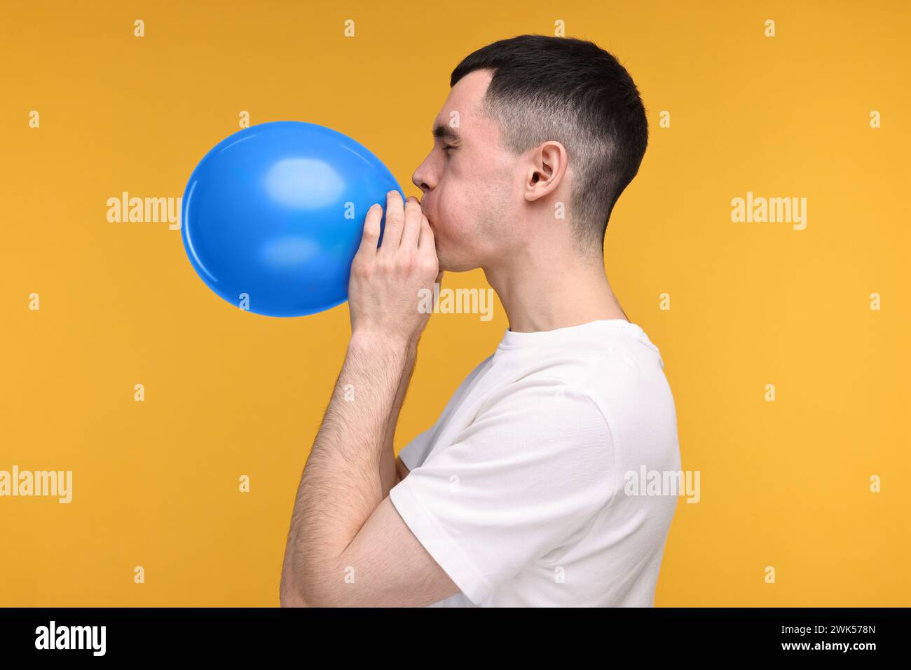 Young man inflating light blue balloon on yellow background Stock Photo ...