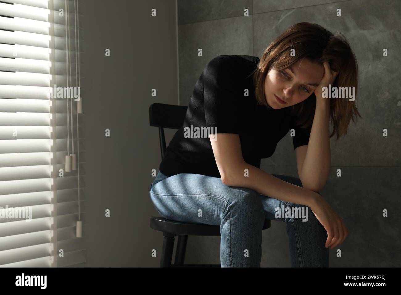 Sad young woman sitting on chair indoors, space for text Stock Photo ...