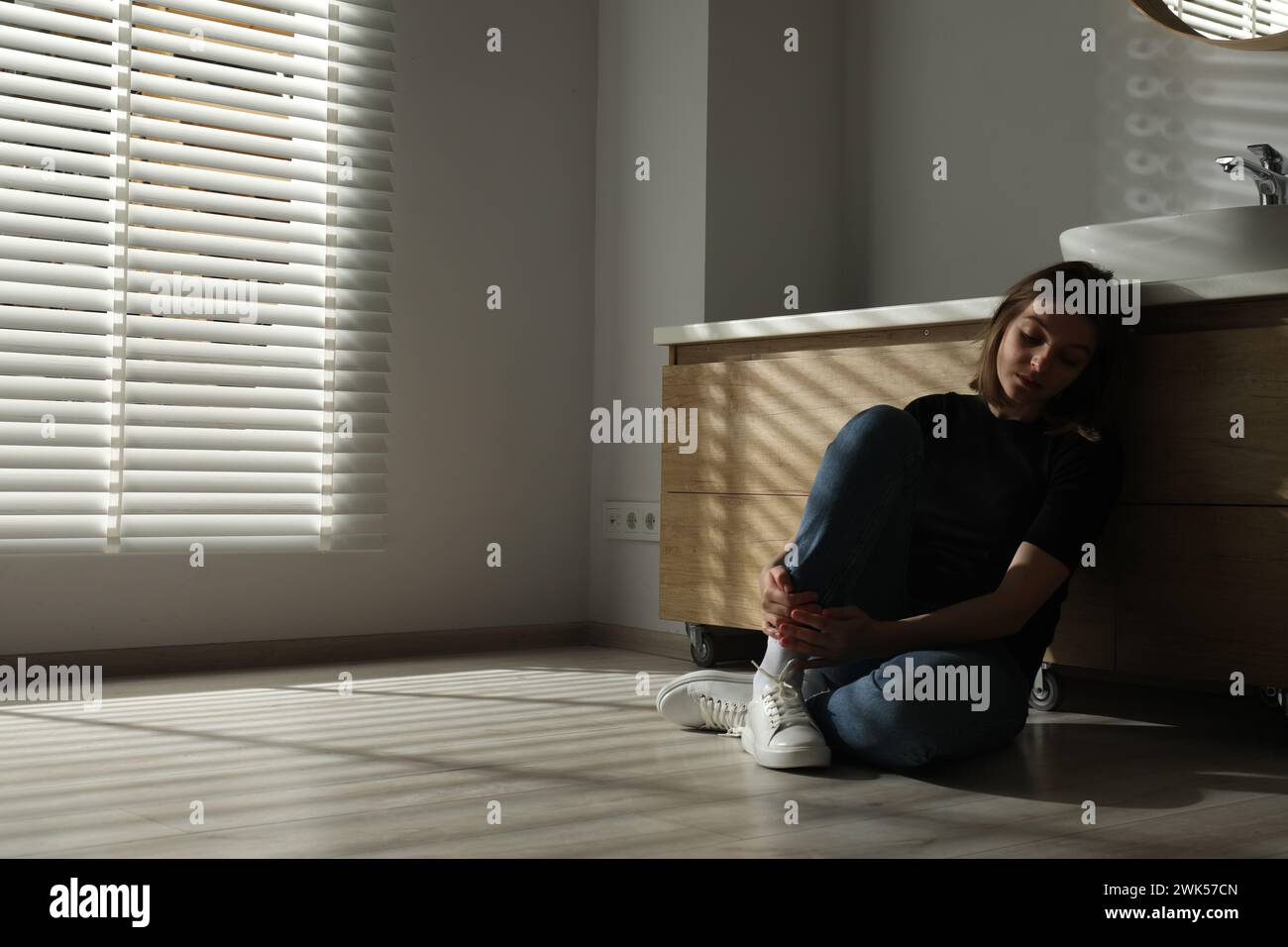 Sad young woman sitting on floor in bathroom, space for text Stock ...