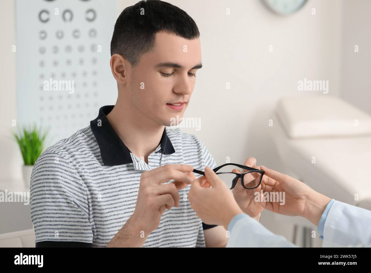 Vision testing. Ophthalmologist giving glasses to young man indoors ...