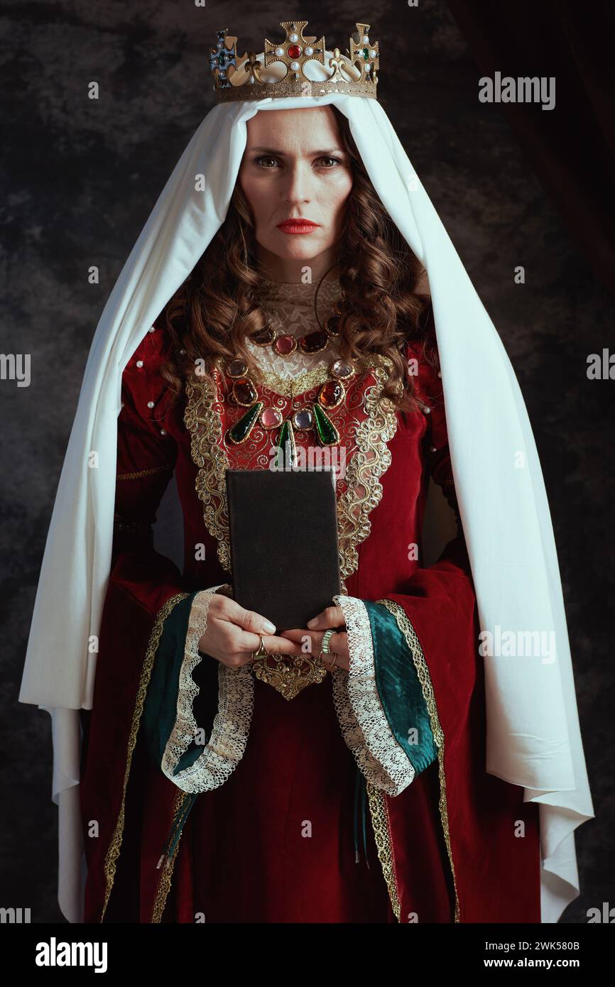 medieval queen in red dress with book, veil and crown on dark gray ...